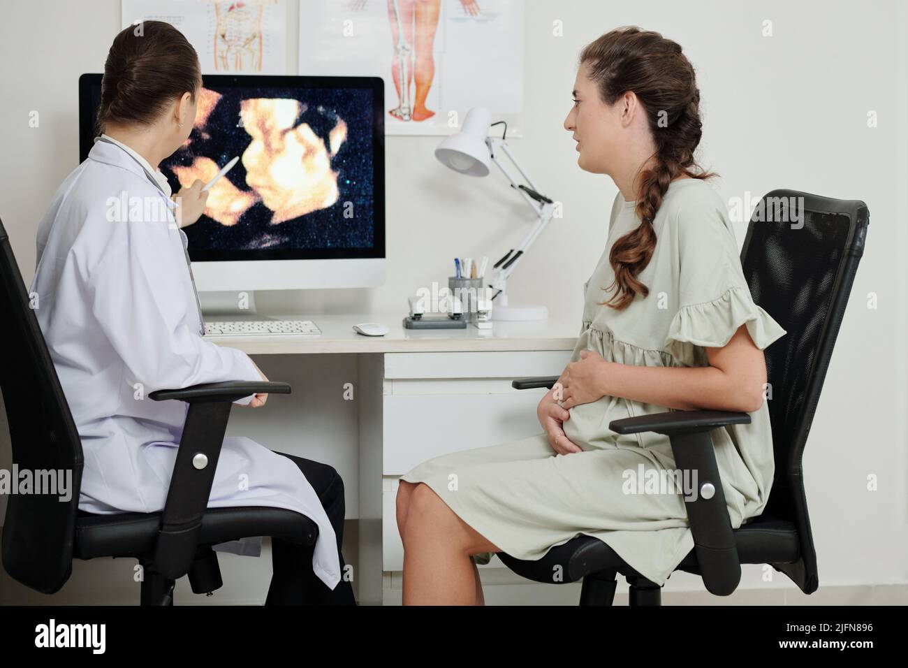 Gynecologist pointing at computer monitor with baby scan and presenting ...