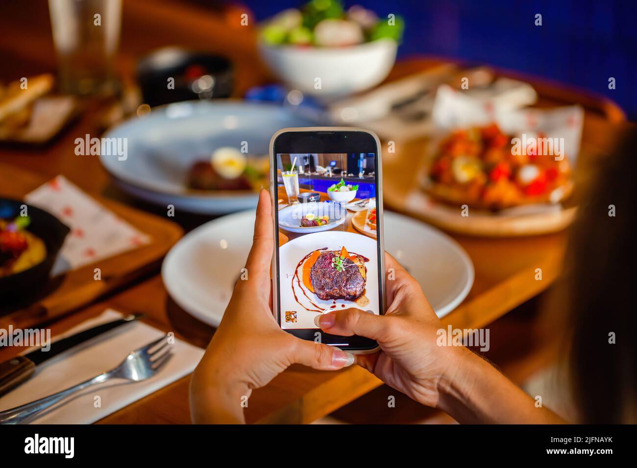 Woman makes mobile phone photo of baked beef meat in luxury restaurant ...