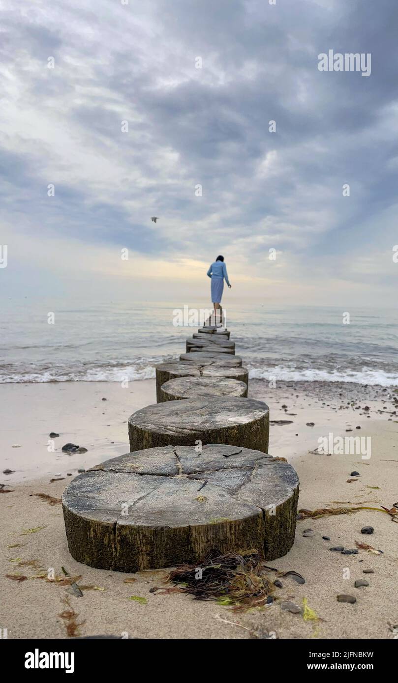 A vertical view of a woman standing on the edge of a breakwater made of ...