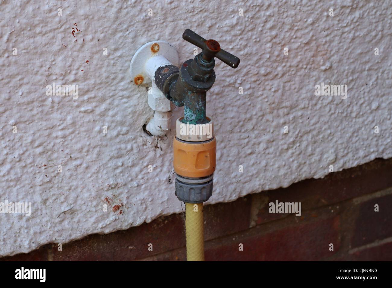 Rusty old metal outside tap connected to a yellow garden hose Stock ...