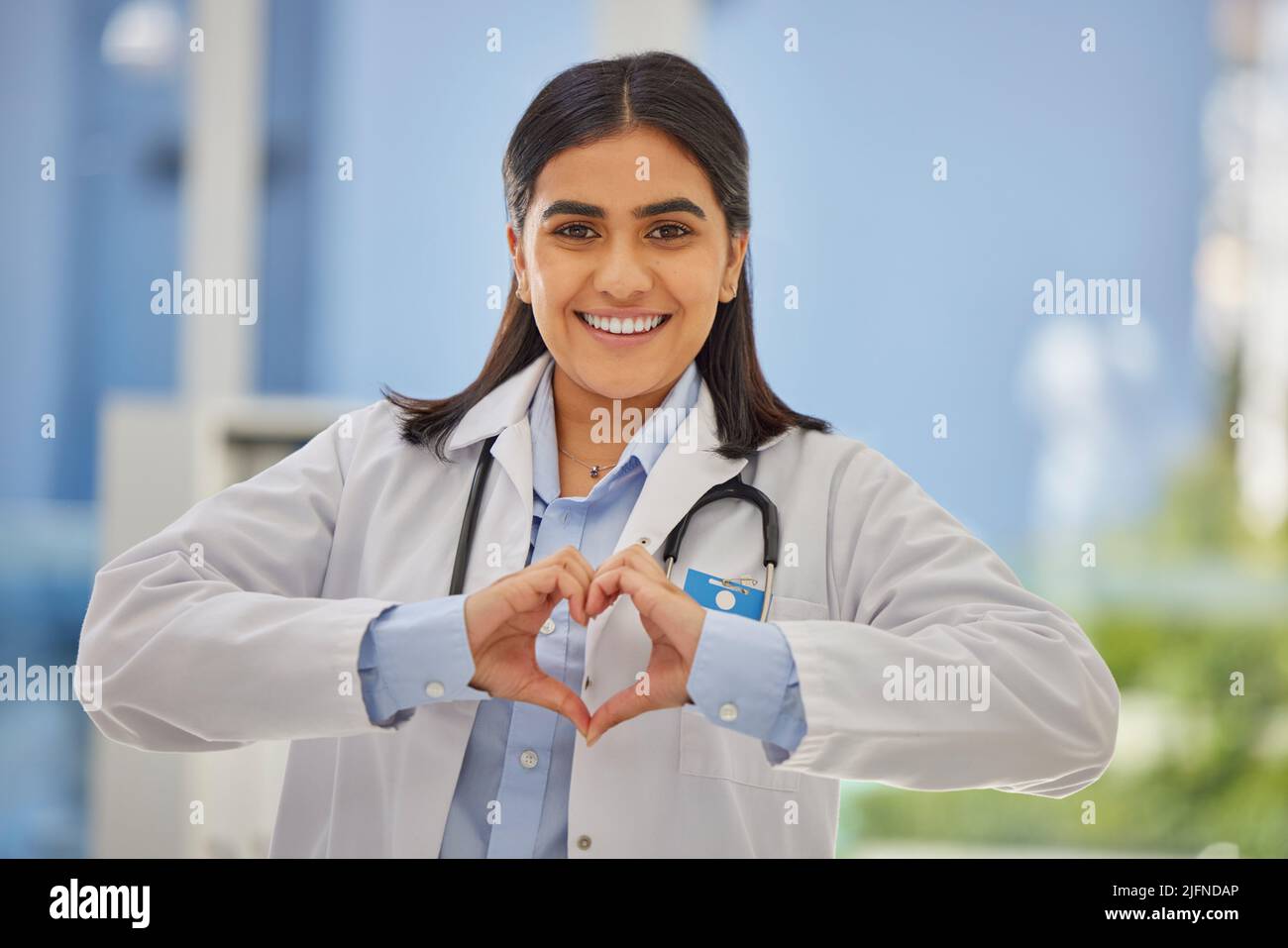 Portrait of a happy mixed race female doctor forming a heart shape with ...