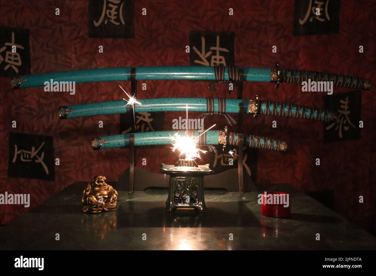 A flame in front of the blue samurai swords on the stand in a room with ...