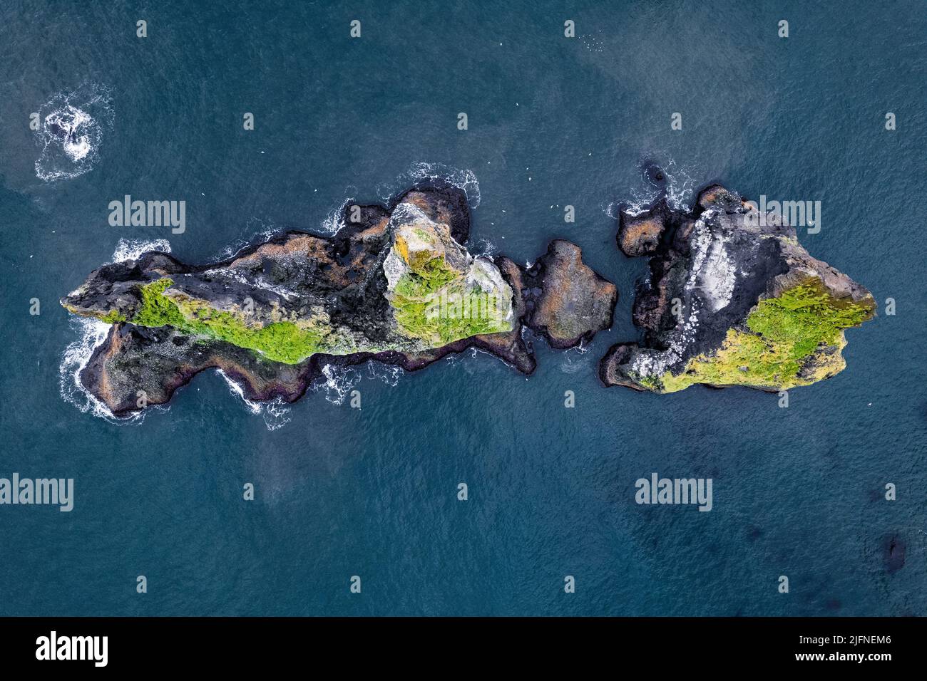 An aerial view of a small island with breaking waves on the stones ...