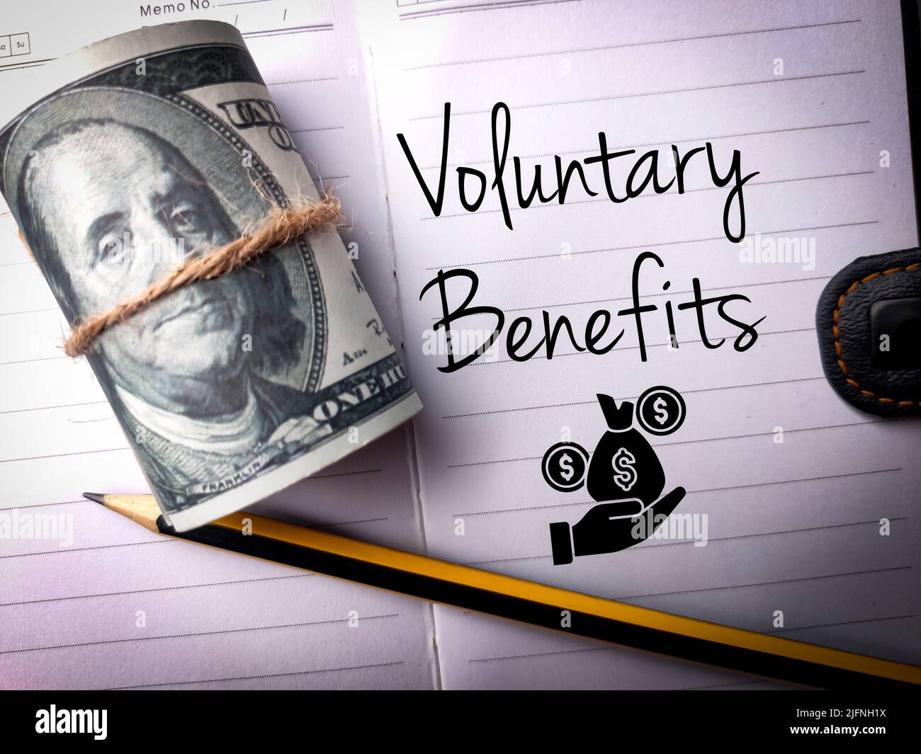 A top view of a pencil, banknotes and a text "Voluntary Benefits" on a ...