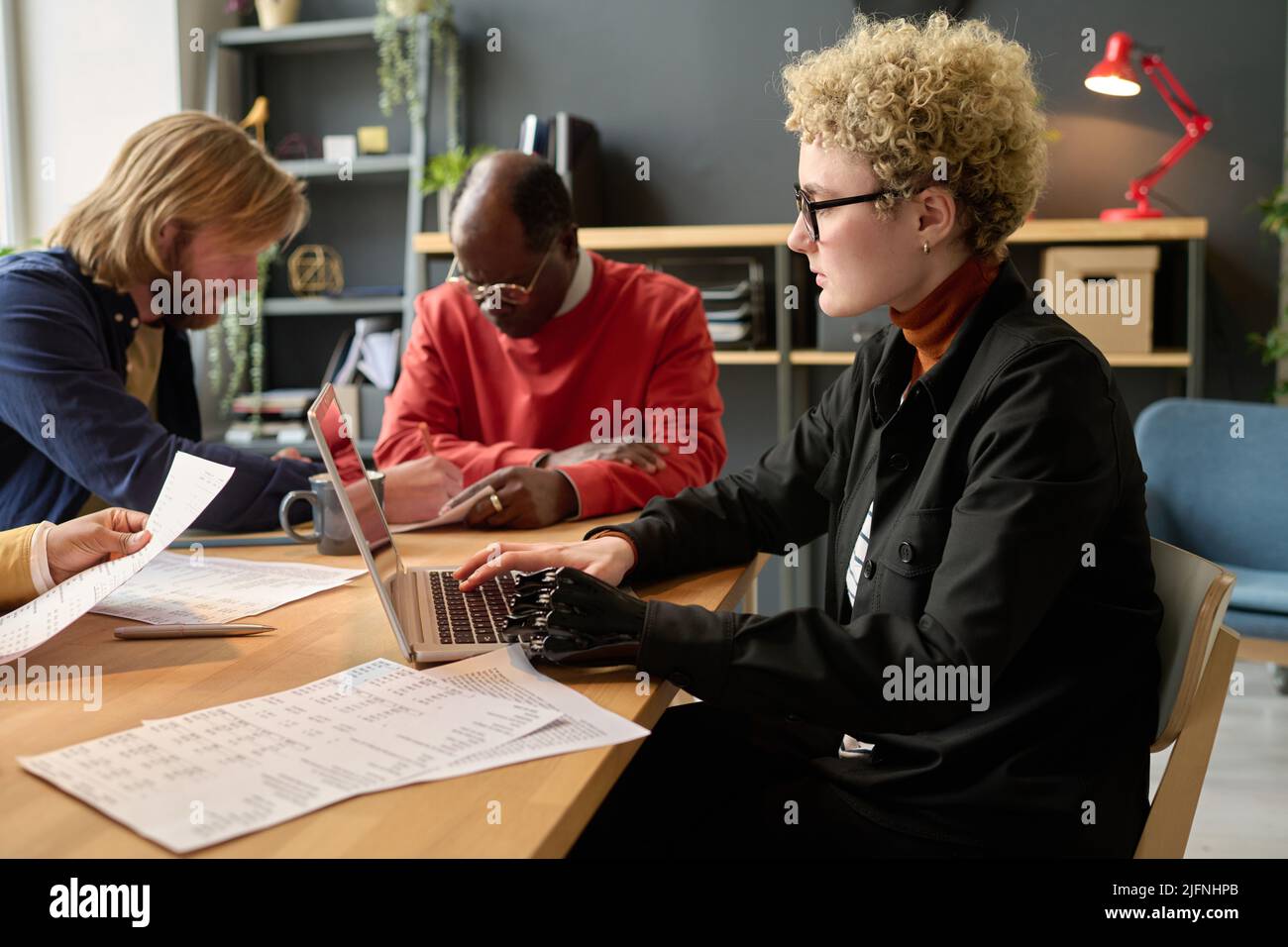 Young businesswoman with prosthetic arm using laptop sitting at table ...
