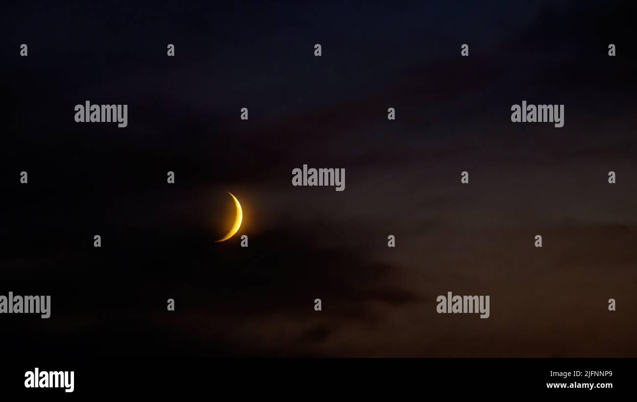 Growing moon in dark cloudy evening sky. Dark colors of summer night ...