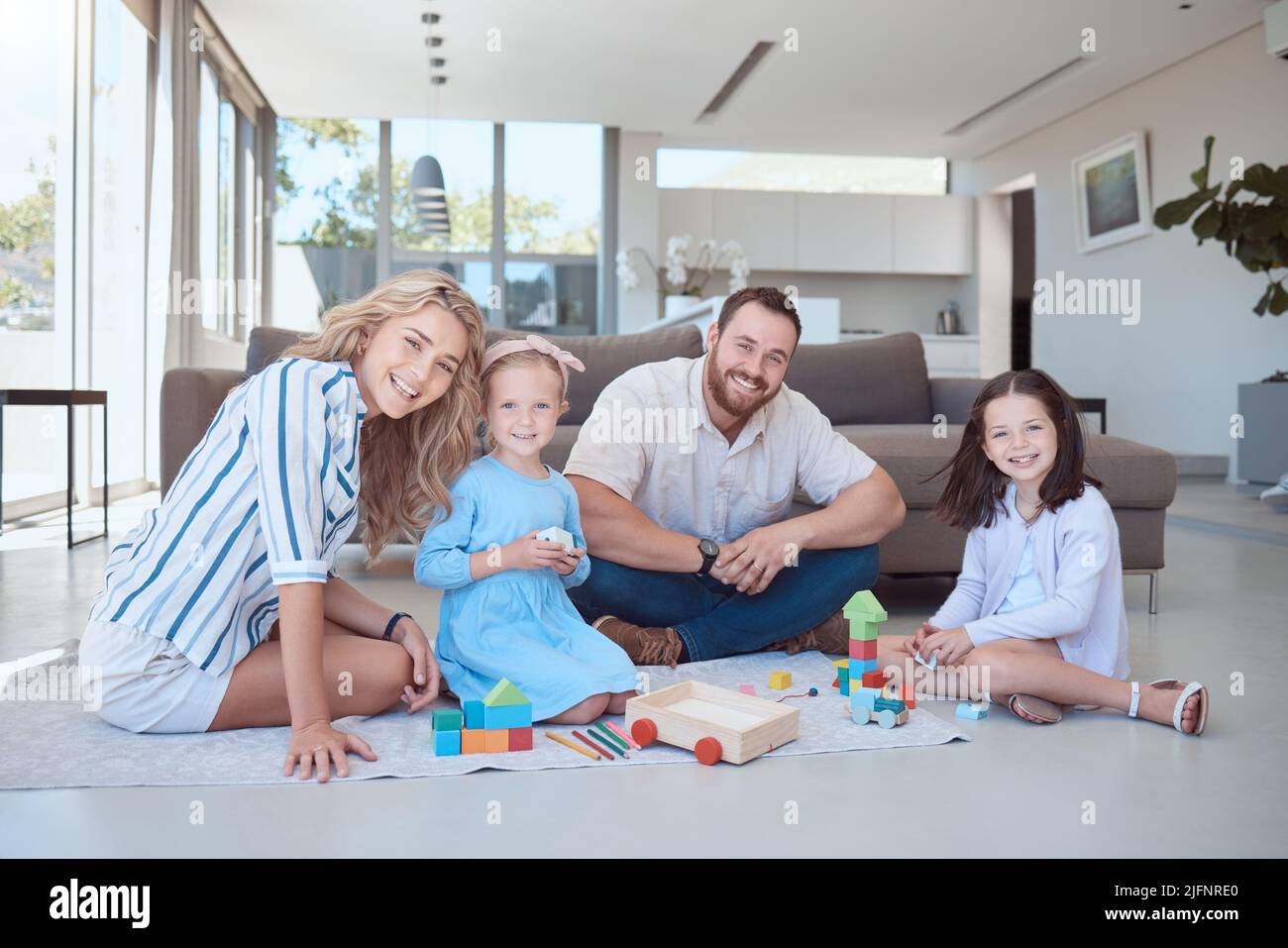 Two little girls playing with colourful building blocks while sitting at home with parents ...