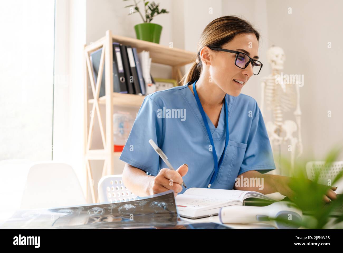 White woman doctor writing down notes while working with laptop in ...