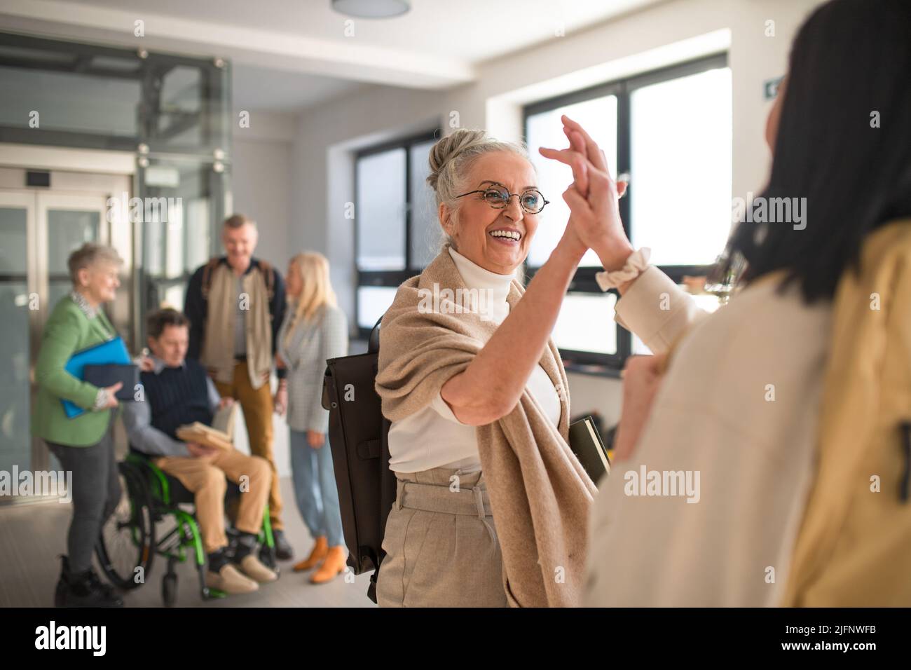 Happy senior women students meeting high fiving in corridor at ...