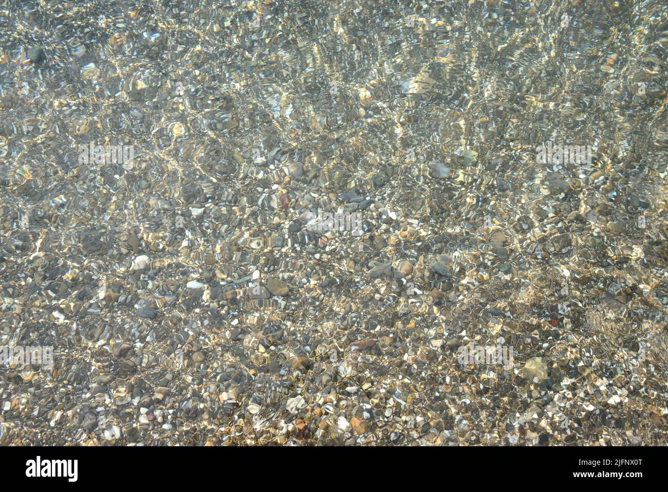 Shimmering sun glares on pebble seabed under clear water of shallow of ...
