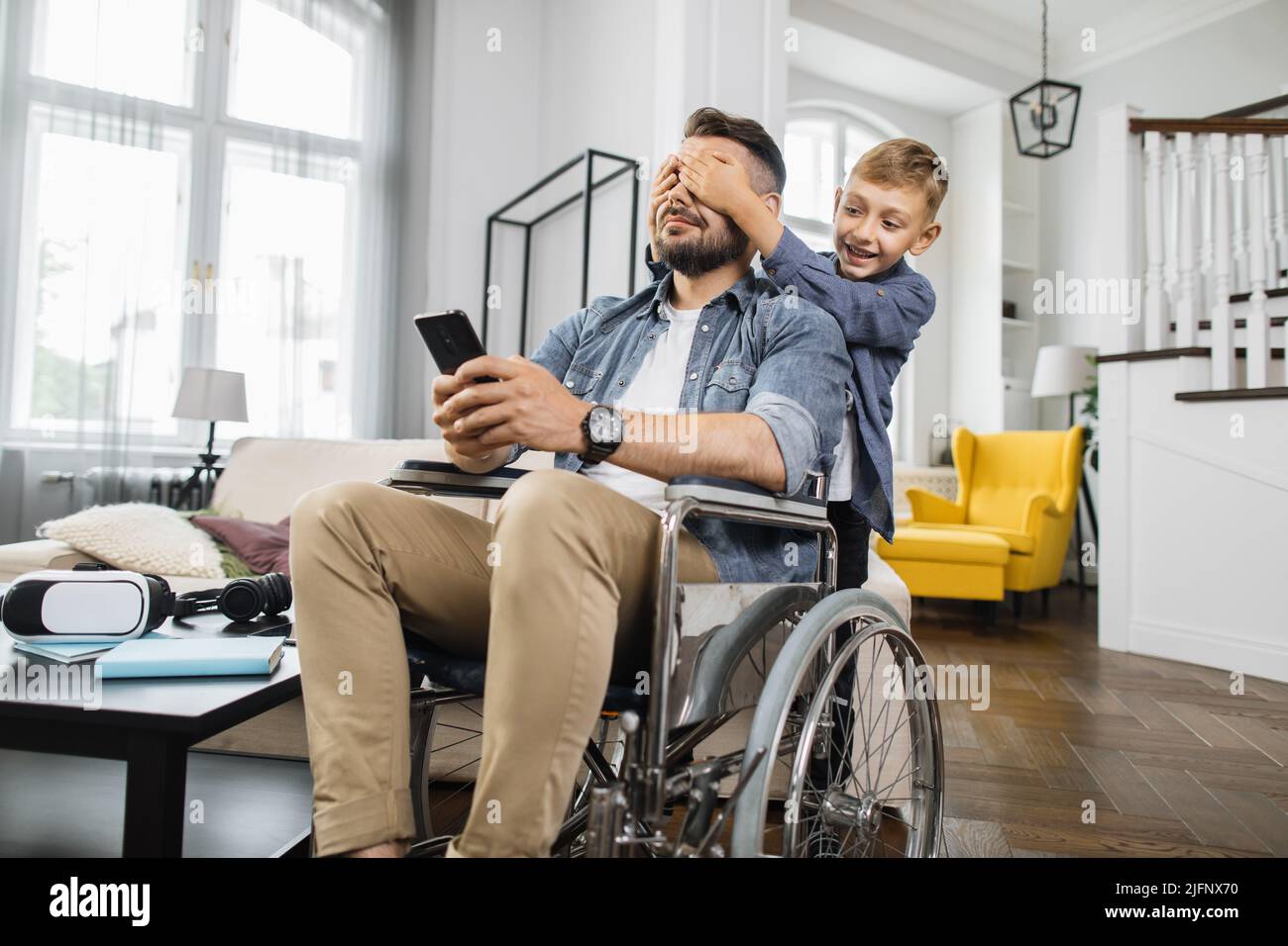 Happy son unexpectedly closing father's eyes from back in modern living ...