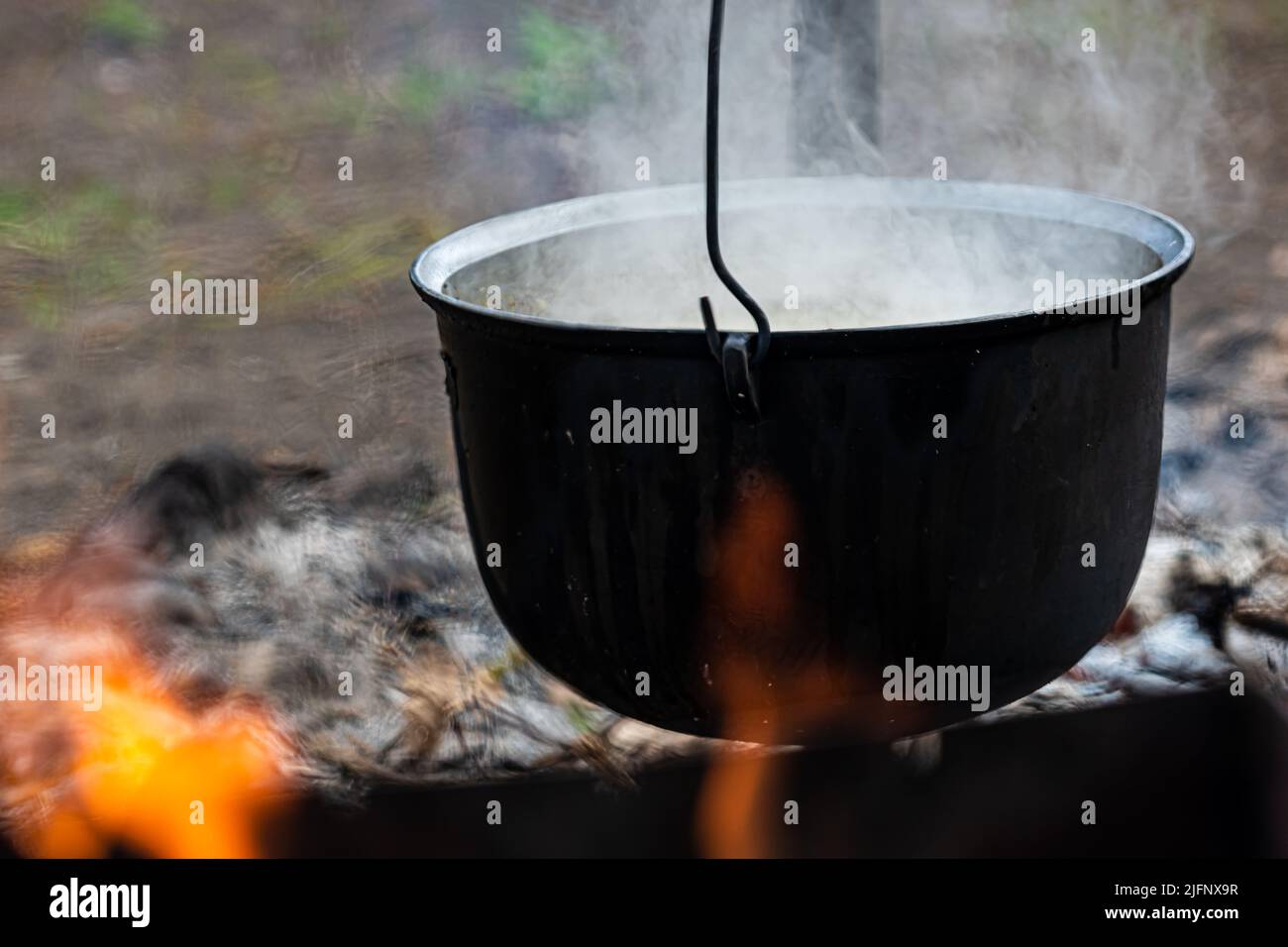 A closeup shot of water boiling in an iron bowl on a bonfire at a camp ...