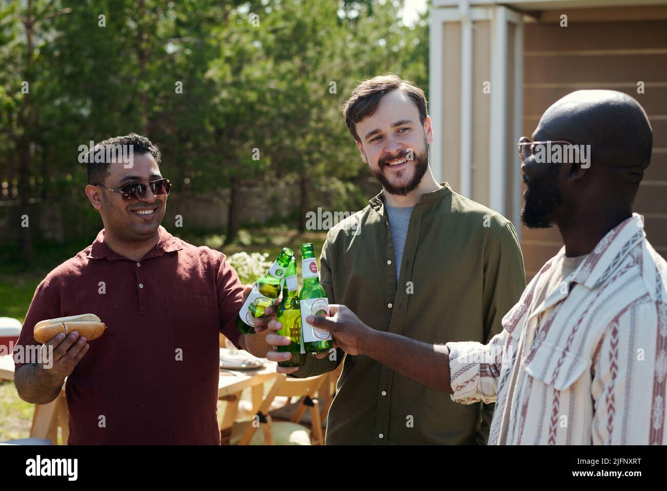 Group of young cheerful intercultural men clinking with bottles of beer ...