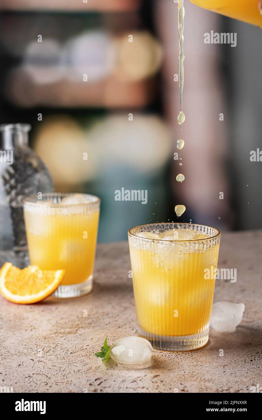Pouring orange juice into a cocktail glass filled with an alcoholic ...