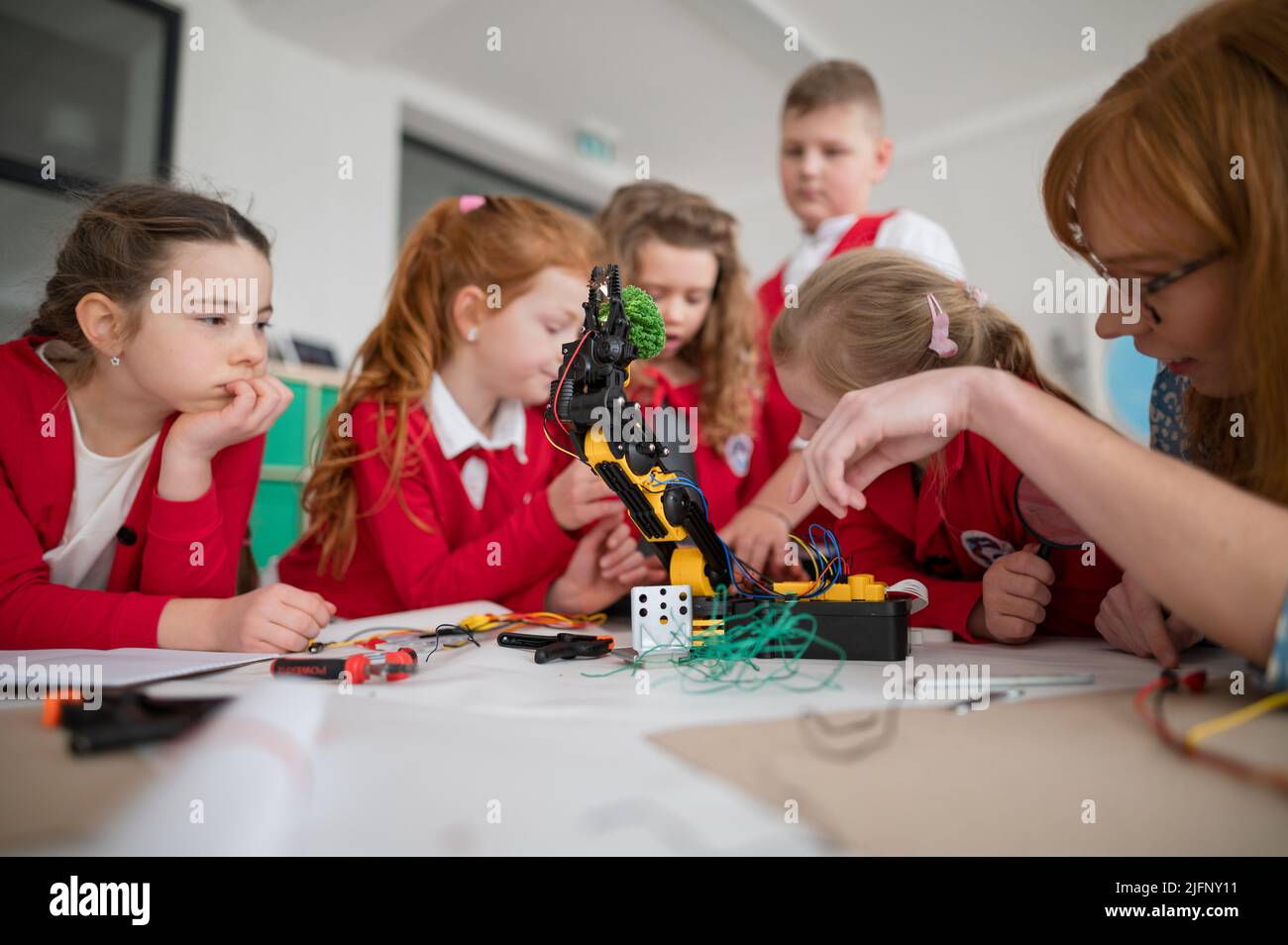 Group of kids with young science teacher programming electric toys and robots at robotics ...