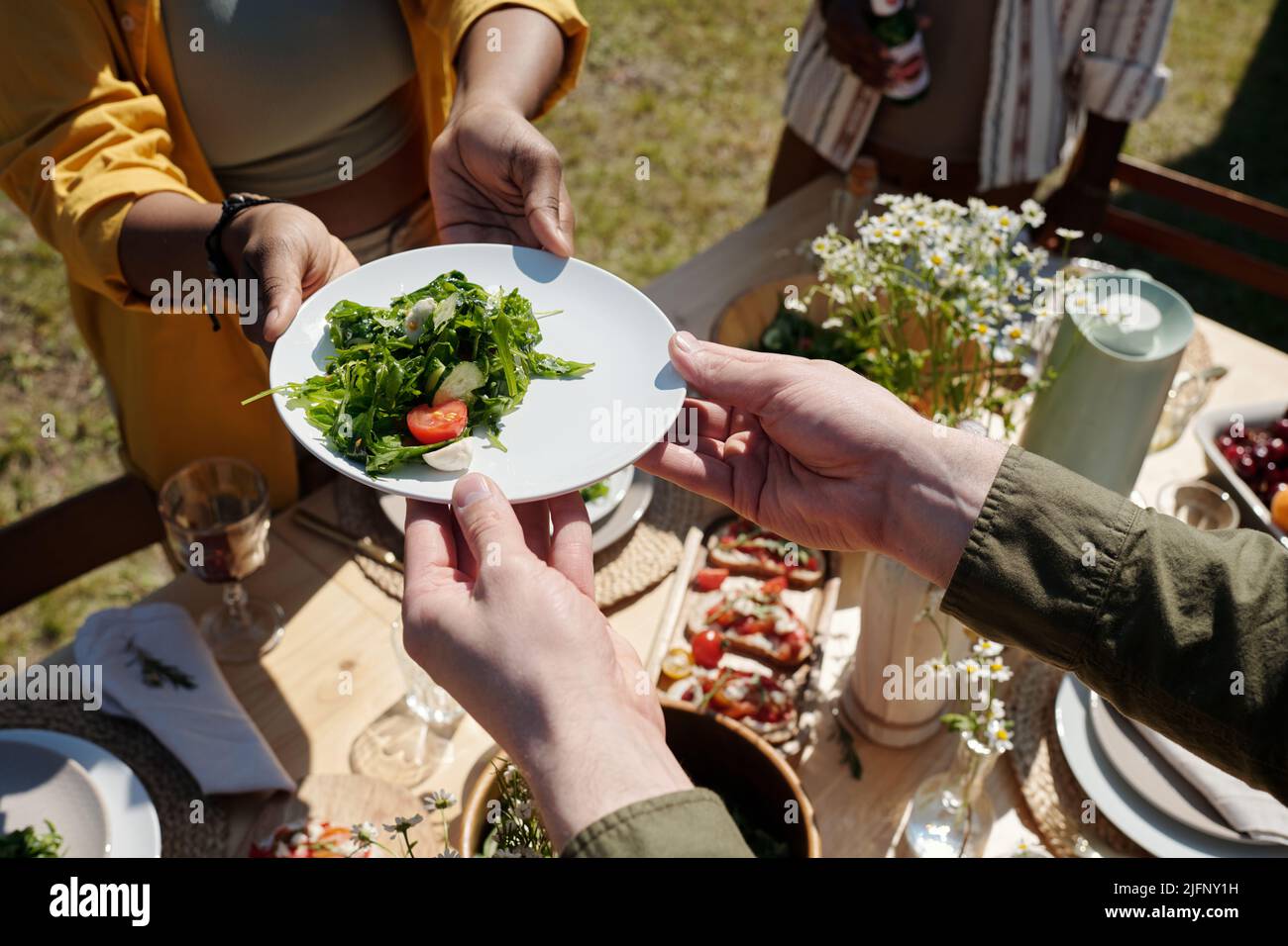 Hands of young man taking plate with vegetable salad being passed by ...