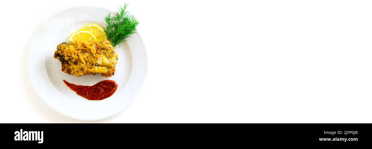 Battered fish on a white ceramic plate with lemon, red sauce and herbs ...
