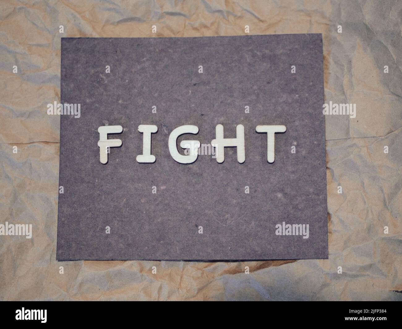 The word FIGHT in wooden lettering on a brown paper baf background ...
