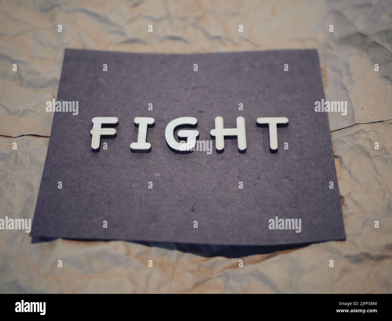 The word FIGHT in wooden lettering on a brown paper baf background ...