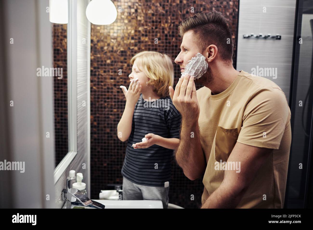 Side view portrait of father and son shaving together and looking in ...