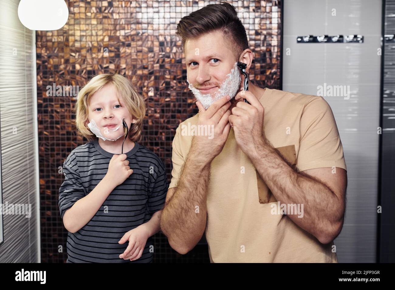 Portrait of happy young father shaving with little boy imitating dad ...
