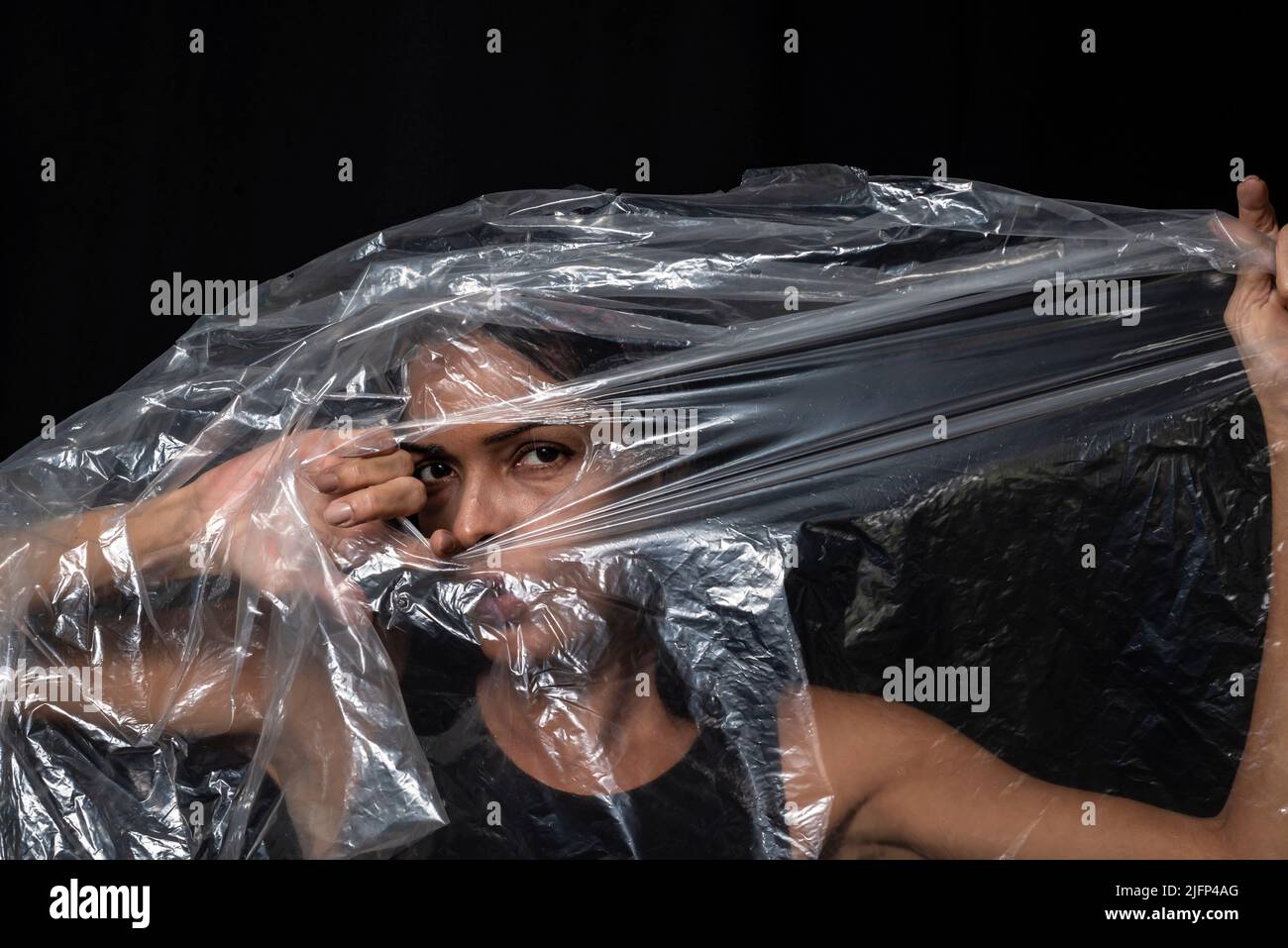 Model portrait with clear plastic in front of her face against black ...