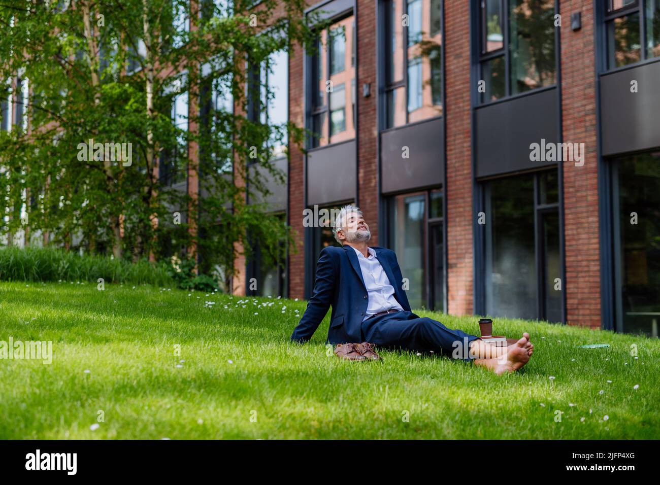 Mature businessman resting and sitting barefoot in park, feeling free ...
