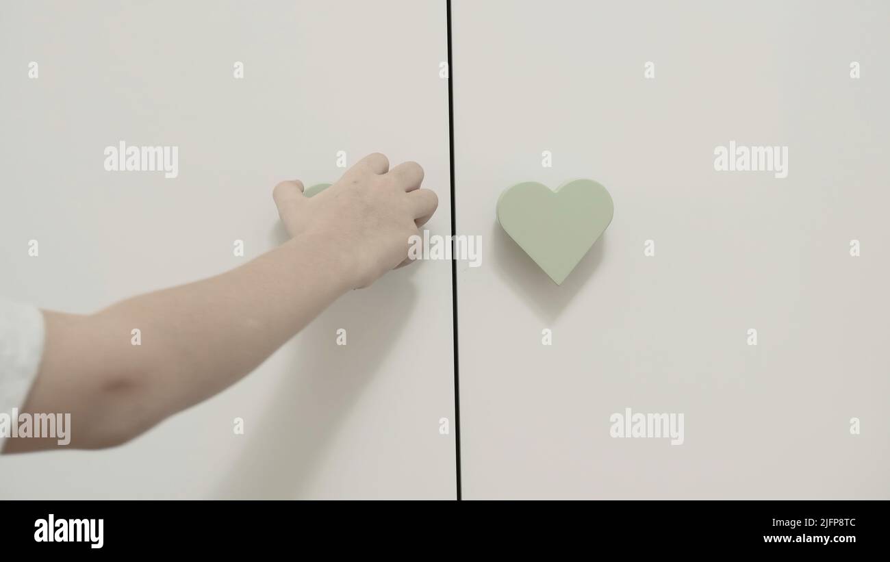 Close up of girl hand opens a door of a white wardrobe with heart shape ...
