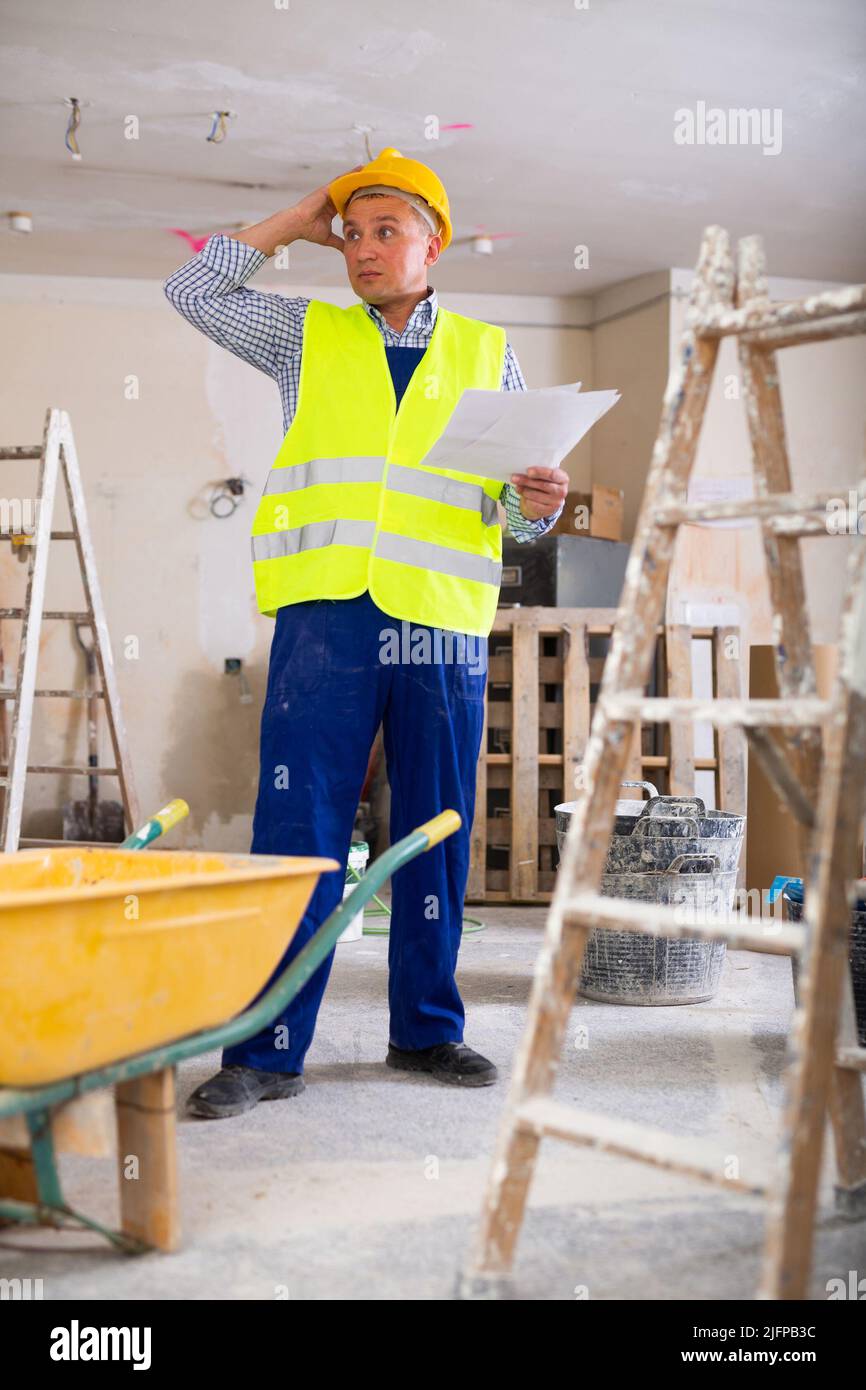 Confused man builder with documentation in apartment Stock Photo - Alamy