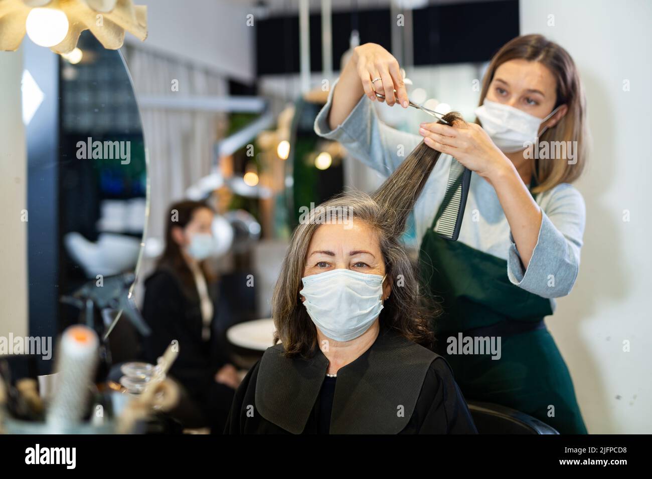 Woman hair stylist in mask making haircut to aged female client Stock ...
