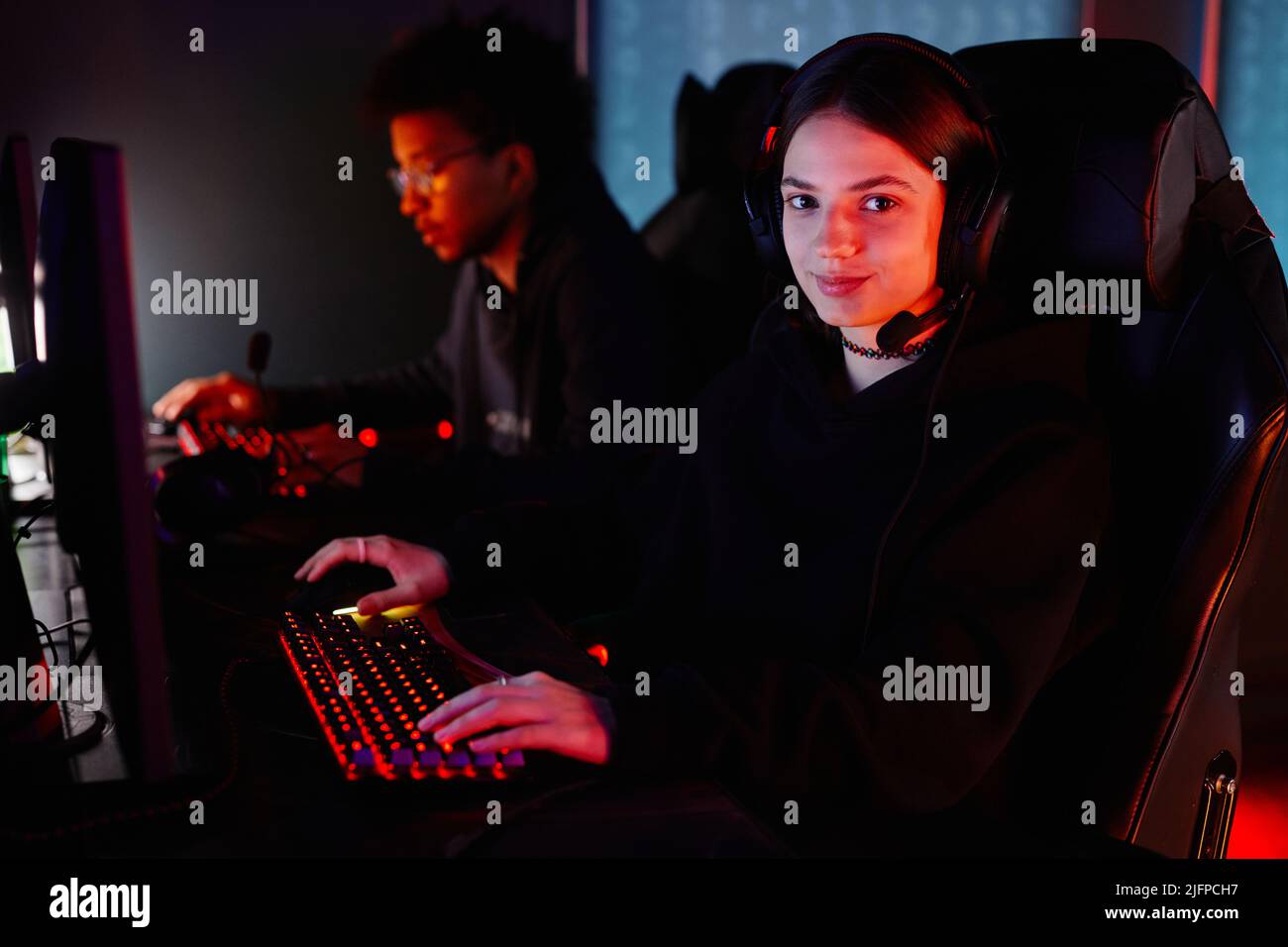 Portrait of female gamer looking at camera in red neon light and ...