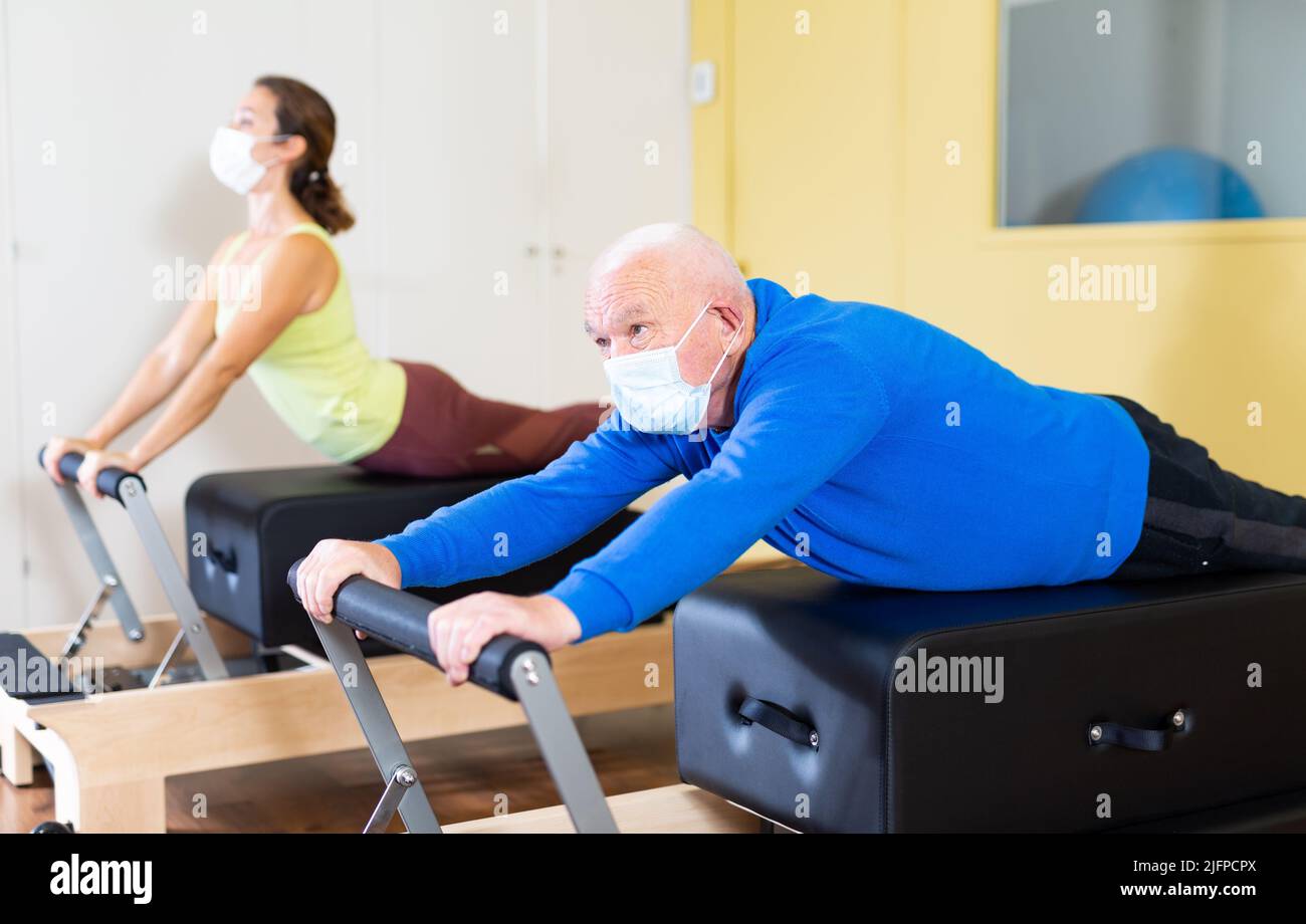 Senior man in medical mask doing stretching exercises on pilates ...