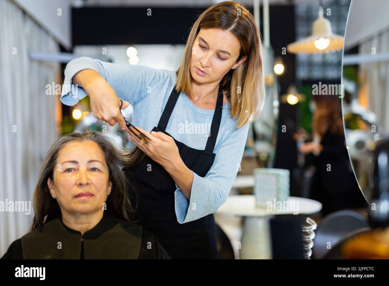 Woman hair stylist making haircut to aged female client Stock Photo - Alamy