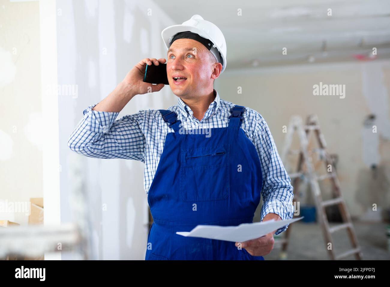 Cheerful man builder having telephone conversation in construction site ...