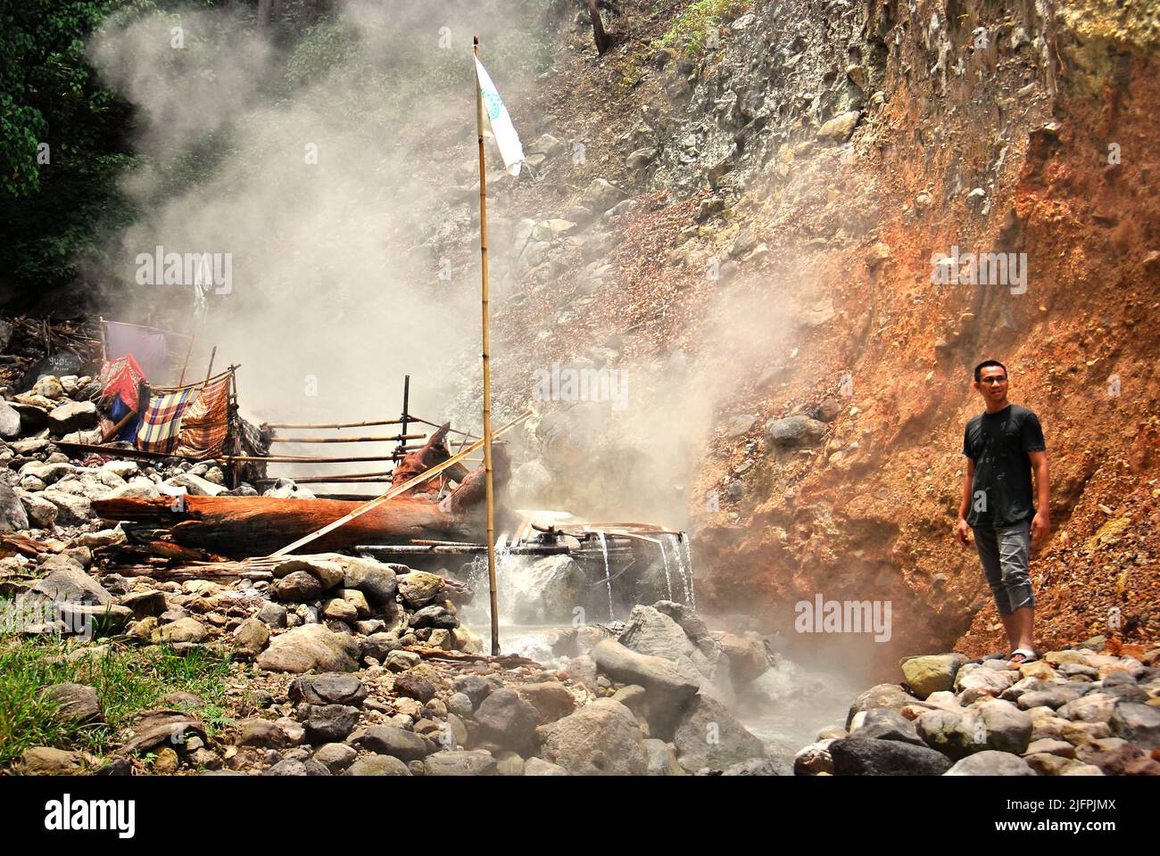 A man standing in front of a hot spring at the foot of Mount Rajabasa ...