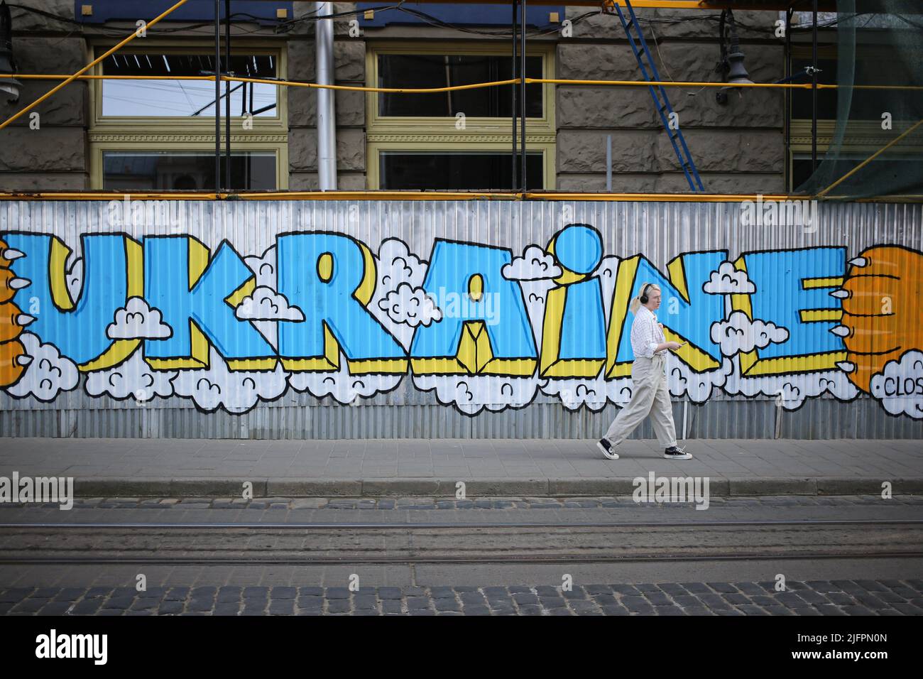 Lviv, Ukraine. 30th June, 2022. A lady walks past a wall with graffiti ...