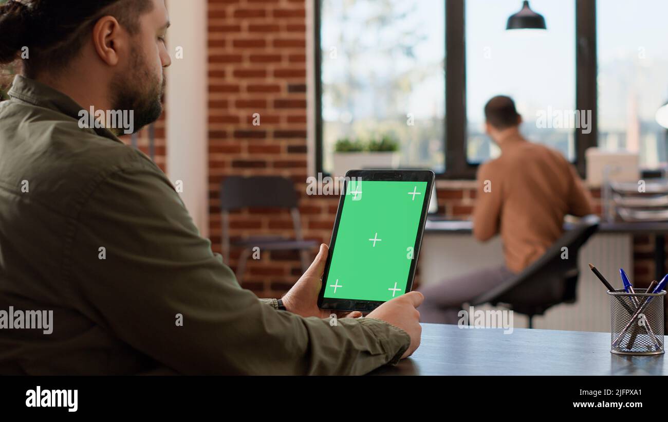 Male freelancer holding digital tablet with greenscreen display, looking at blank chroma key ...
