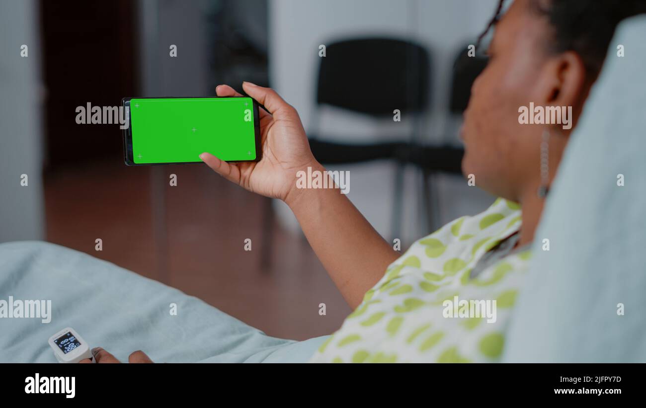 Sick patient holding smartphone with horizontal green screen in ...