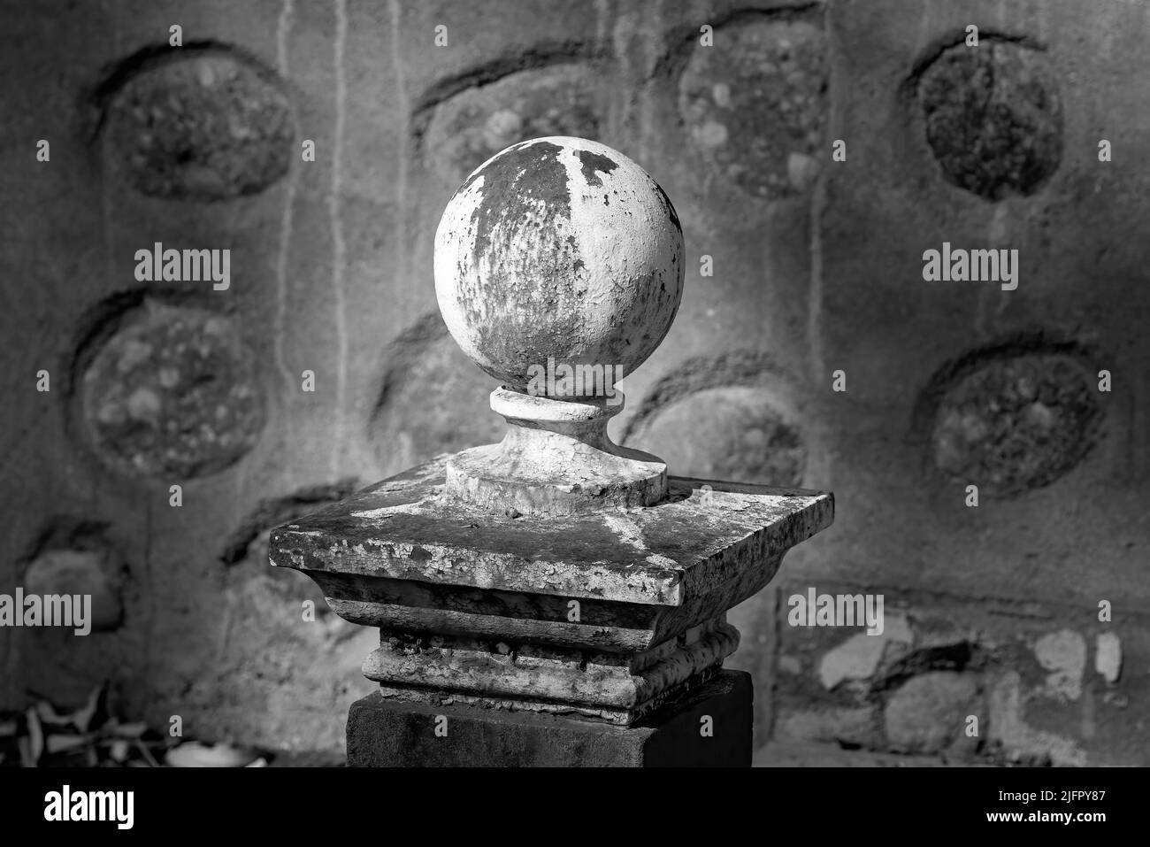 An old round concrete globe statue pitted with age, situated at the ...