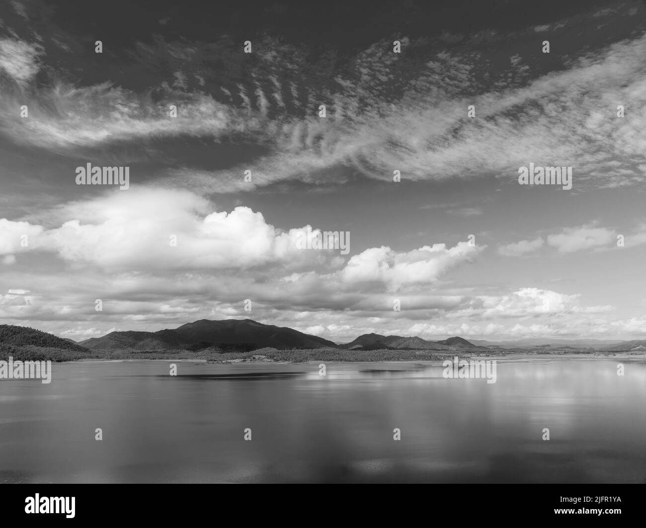 The calm flat blue waters of a dam with the cloud formations reflected ...