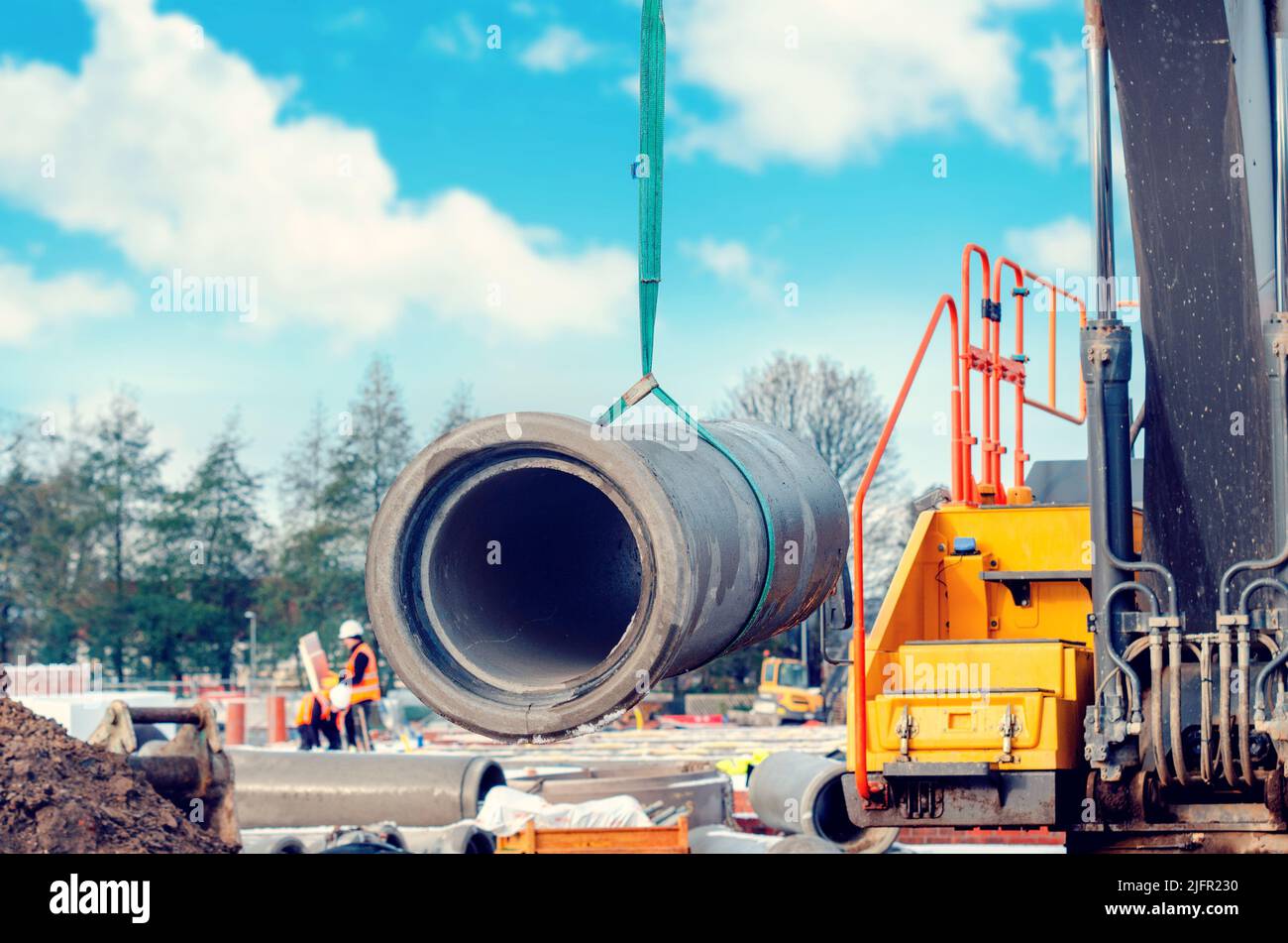Concrete drainage pipe lifted by excavator during deep drainage works ...