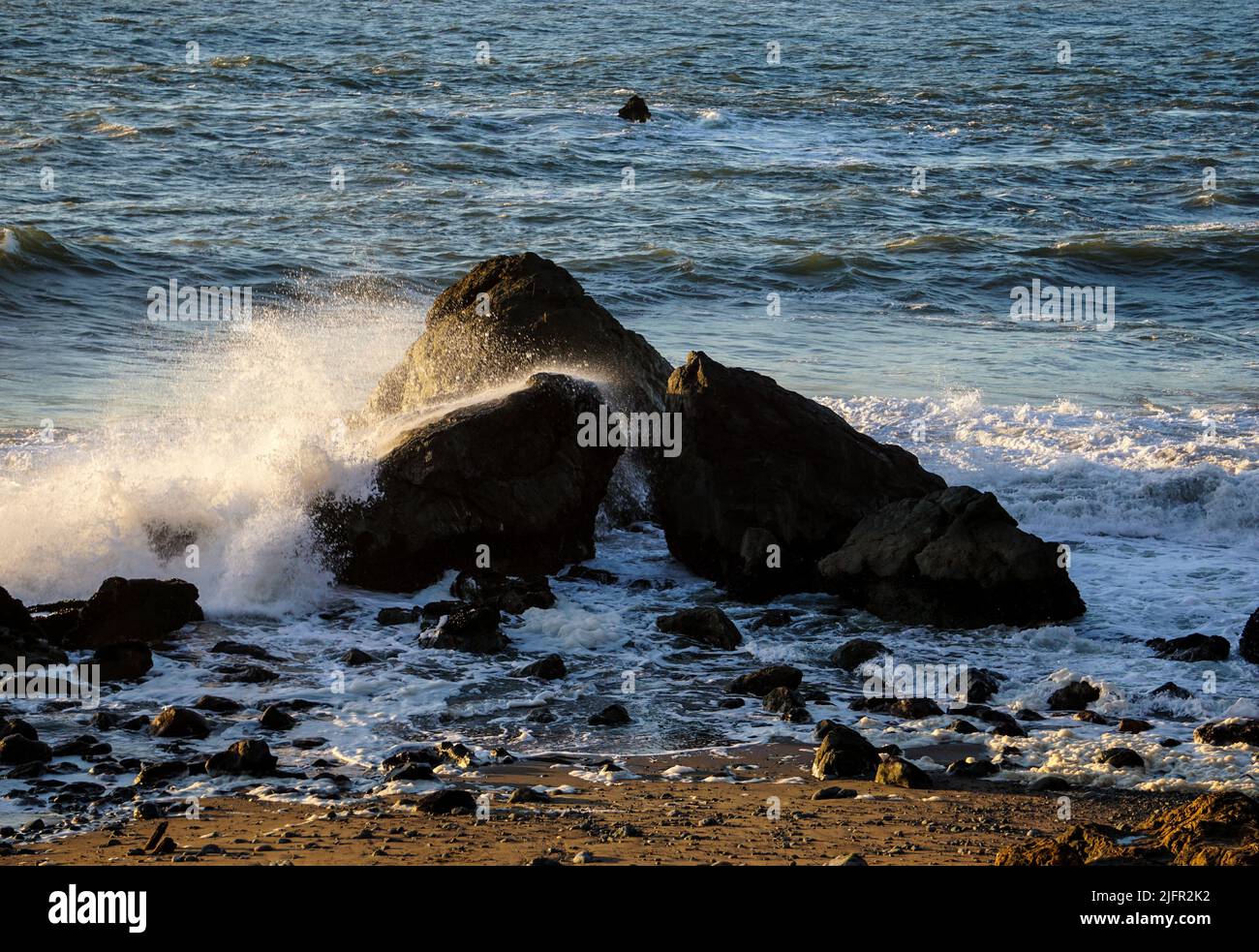 A scenic view of ocean waves hitting the rocks on the beach in daylight ...