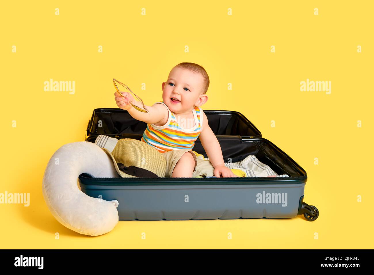 Baby toddler boy sits inside a suitcase with clothes, studio yellow ...