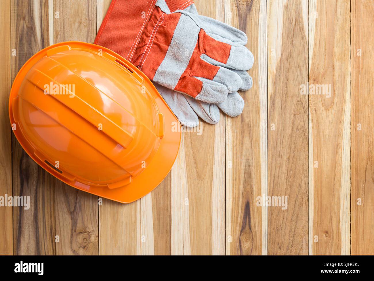 Orange safety engineer helmet gear and gloves on top of brown wooden ...