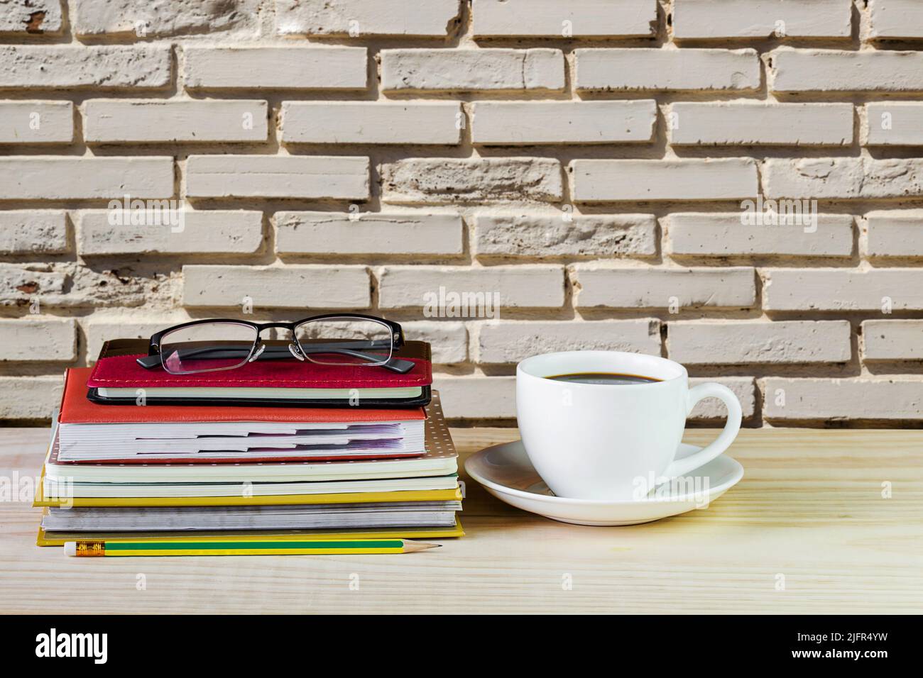Coffee cup, glasses, and stack of book on wooden table with blur wall ...