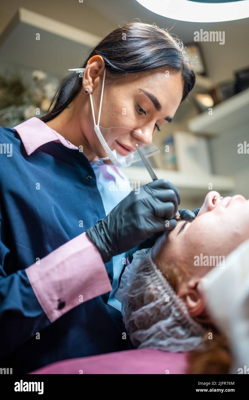 Procedure of eyebrow microblading. A master in black gloves is doing a ...