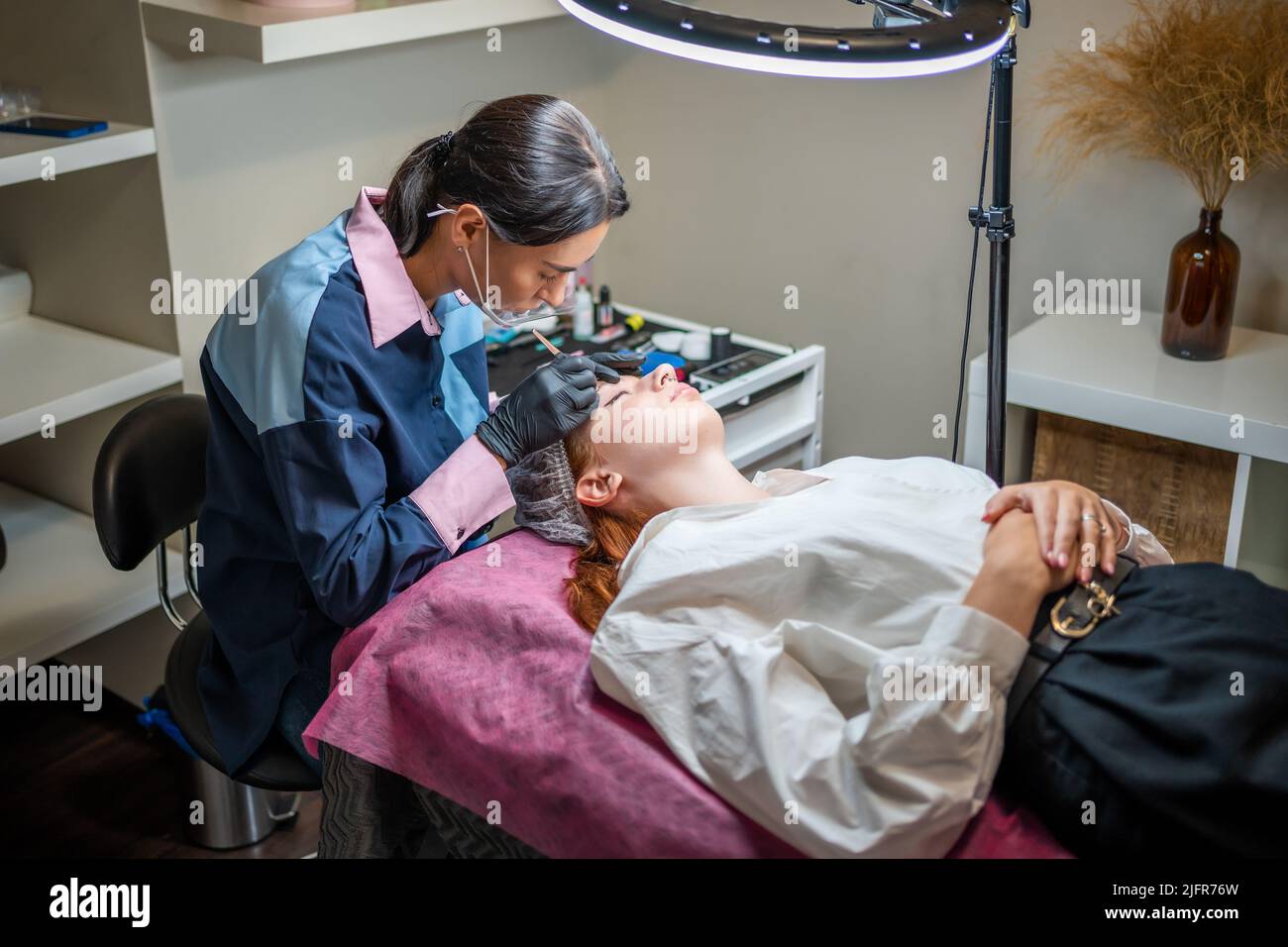 Procedure of eyebrow microblading. A master in black gloves is doing a ...