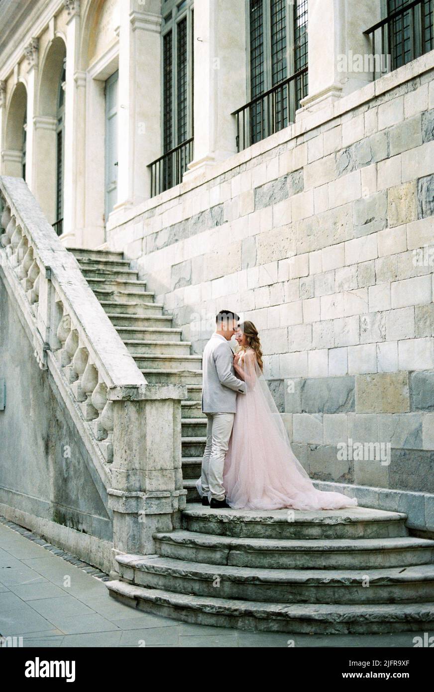Bride and groom are standing on the stone steps of an old building ...