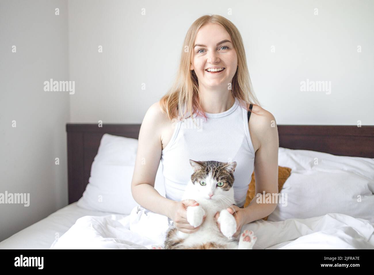 Portrait of young blonde happy 30s woman holding unhappy cat with green ...