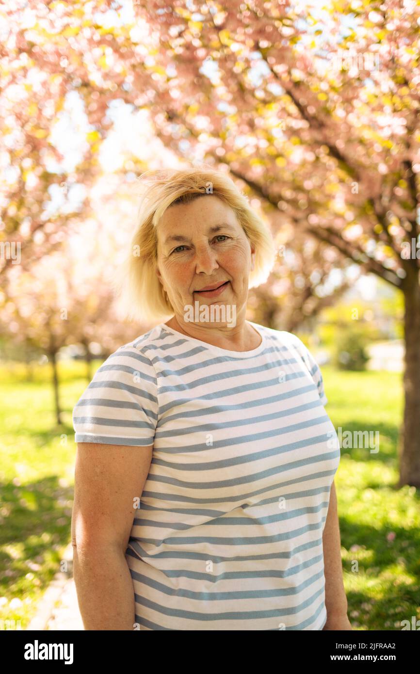 Beautiful cute blonde 50s woman near the tree blossoms with pink ...